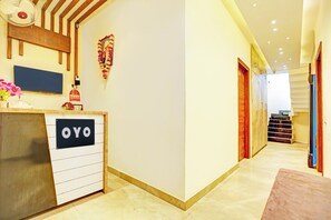 Uma área de recepção de hotel com um balcão de madeira, uma placa com a inscrição 'OYO' e uma escadaria que leva a outro andar.