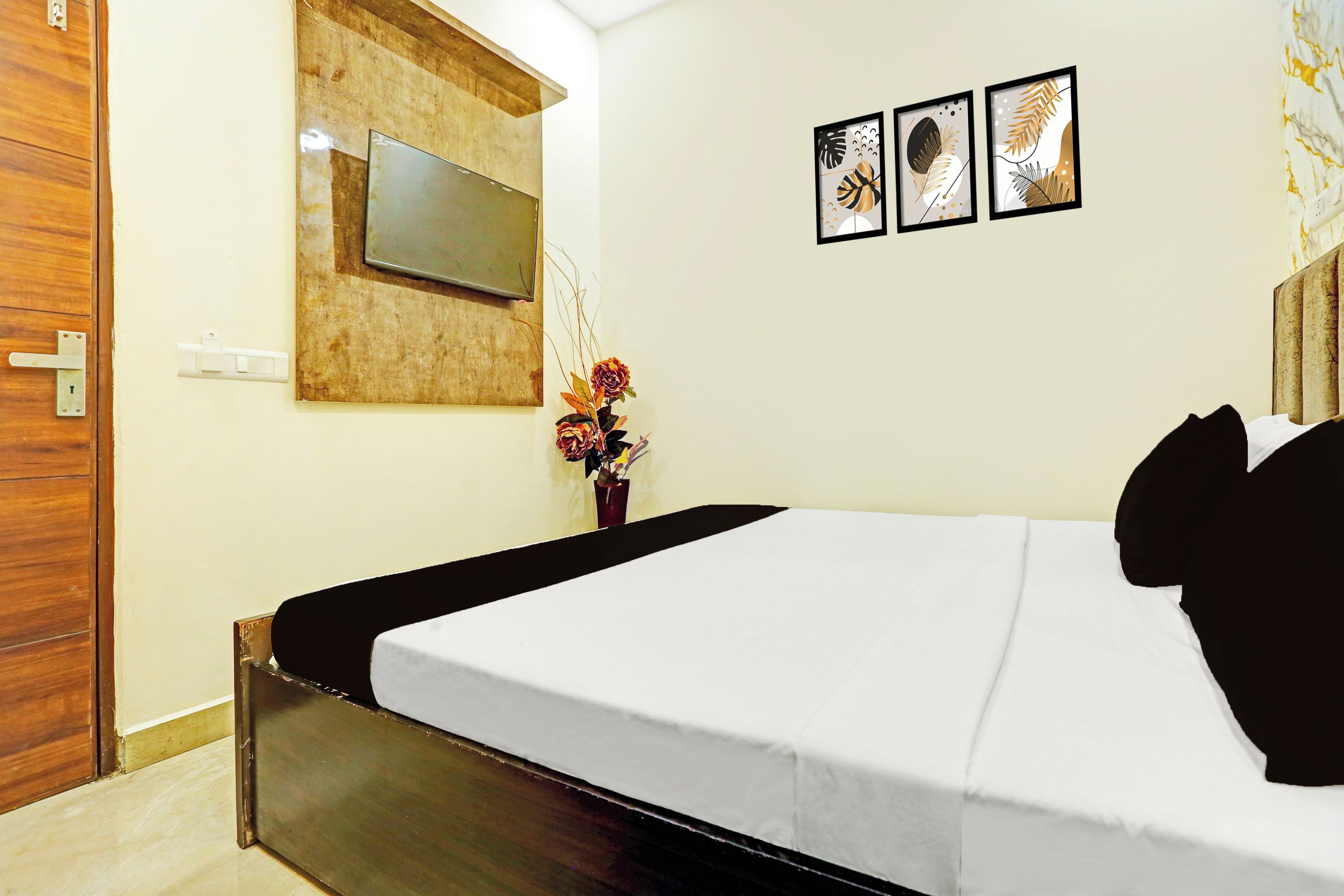 Quarto de hotel com cama, televisão na parede e uma mesinha com um vaso de flores.