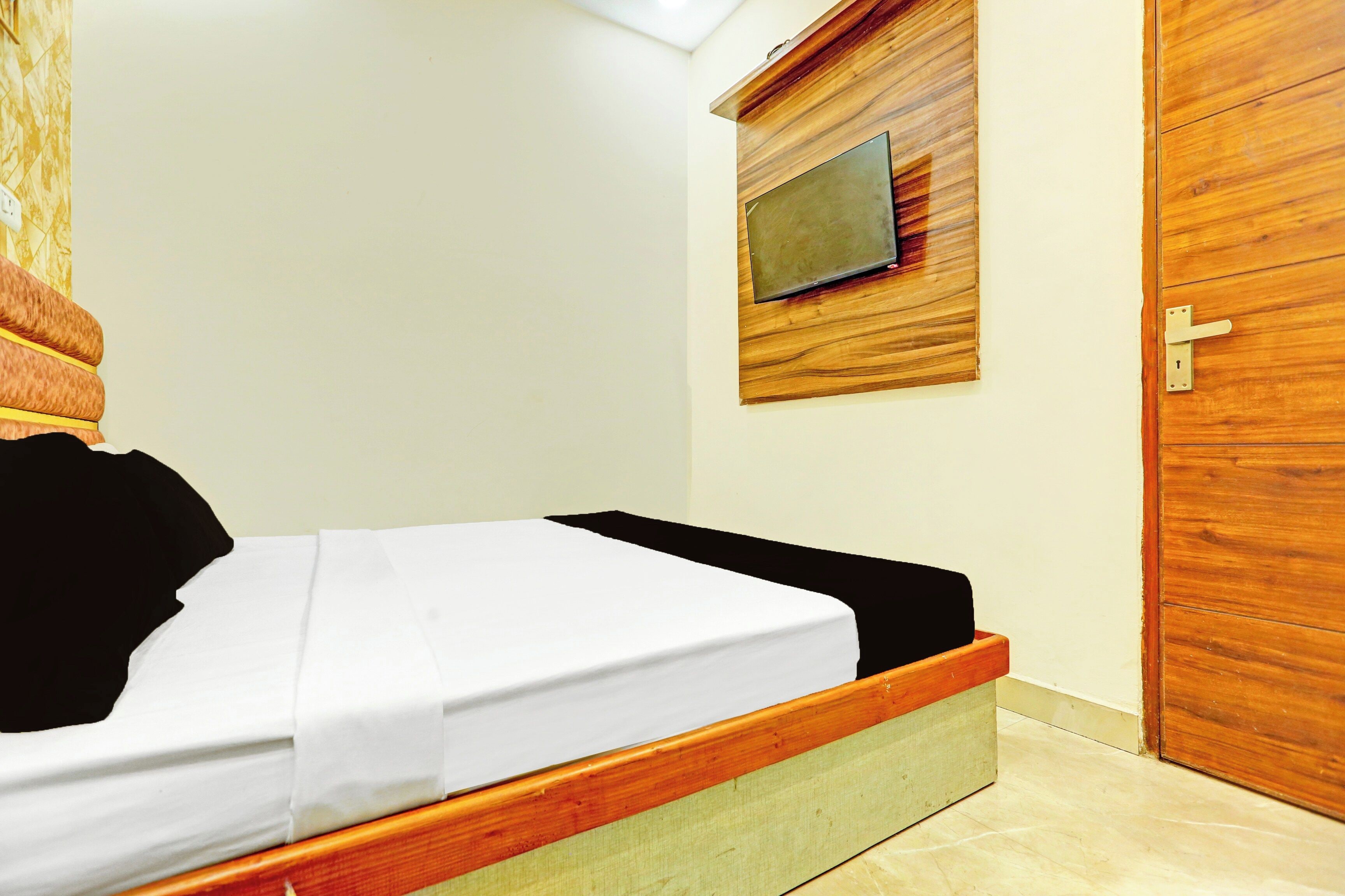 Quarto com cama, porta de madeira e televisão presa na parede.