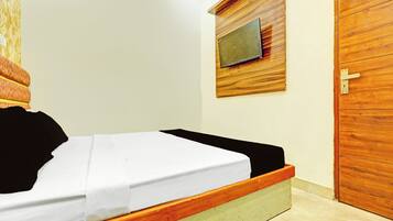 Quarto com cama, porta de madeira e televisão presa na parede.