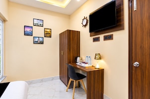 Quarto de hotel com uma cama, escrivaninha com cadeira, televisão e guarda-roupa.