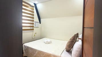 Quarto pequeno com uma cama de solteiro, guarda-roupa de madeira, janela com persianas e mesa de cabeceira com abajur.