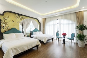 Quarto de hotel com duas camas, área de estar com mesa e cadeiras, e uma janela grande com cortinas.