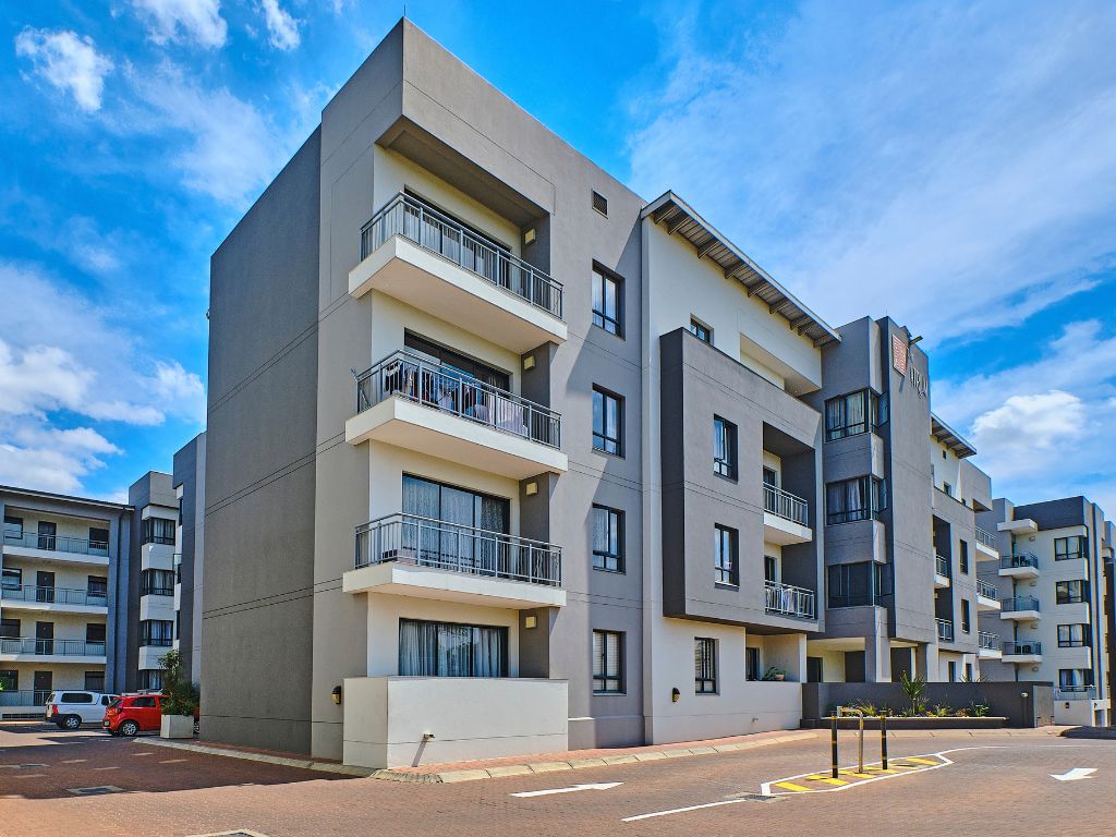 Um edifício residencial com vários andares, varandas, área de estacionamento e céu claro.