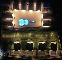 Vista aérea de um hotel com um pátio central que apresenta uma instalação de luz em formato de guitarra, rodeado por vários quartos com áreas de estar ao ar livre.