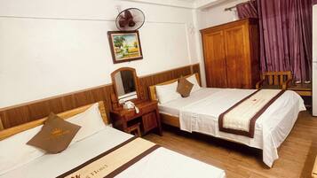 Quarto de hotel com duas camas de solteiro, um guarda-roupa de madeira, uma escrivaninha com telefone e um ventilador fixado na parede.