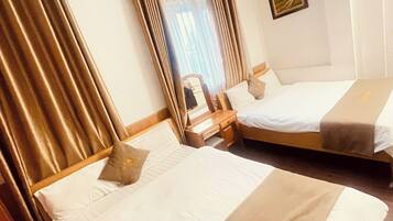 Quarto de hotel com duas camas, cabeceira de madeira, janela com cortinas, um quadro na parede e teto com claraboias.