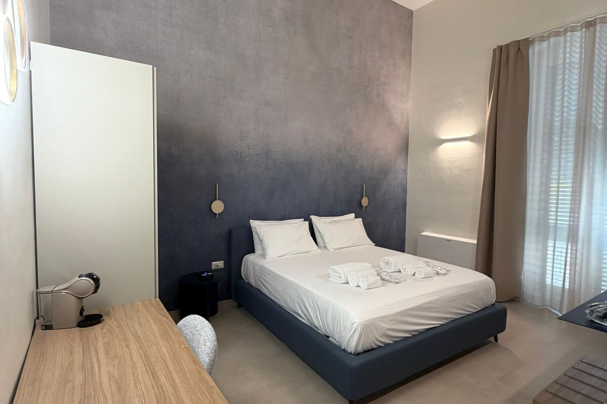 Quarto moderno com cama grande, mesas de cabeceira, escrivaninha e um espelho amplo.