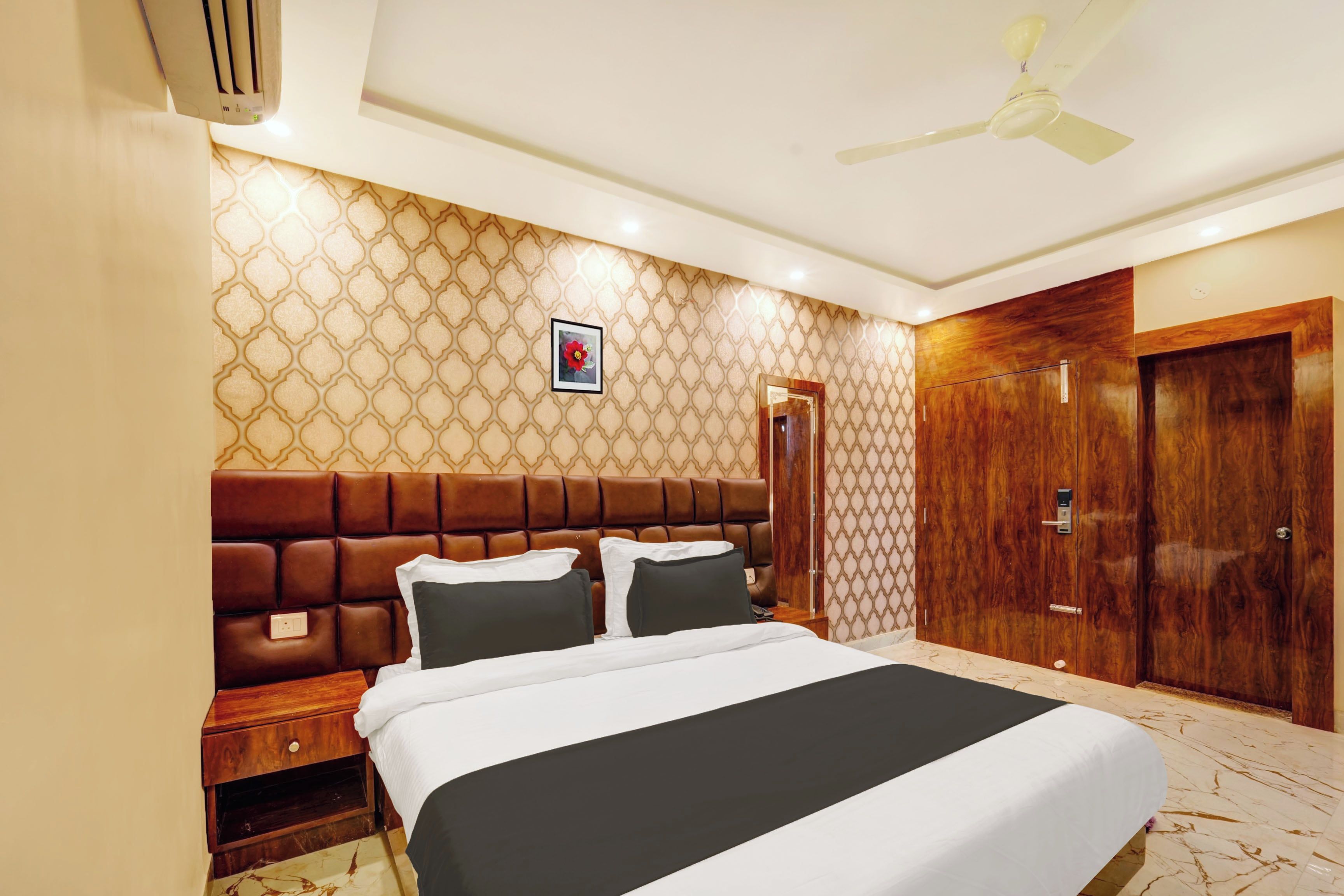 Quarto de hotel com uma cama grande, cabeceira de madeira, guarda-roupa e ventoinha no teto.