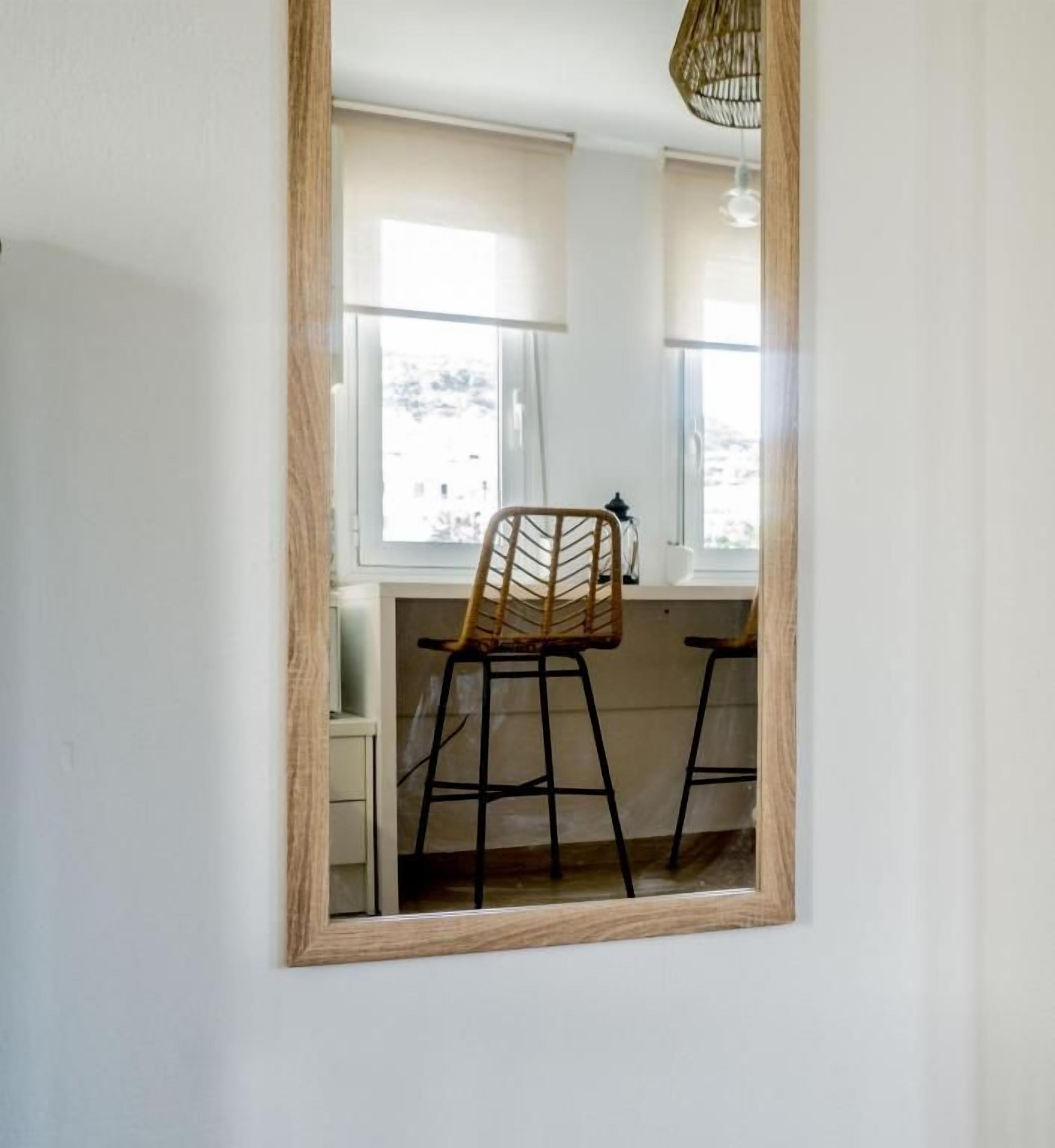 Quarto com um espelho grande refletindo uma cadeira e uma janela.