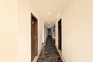 Corredor com portas de madeira, chão de mármore e luminária no teto.