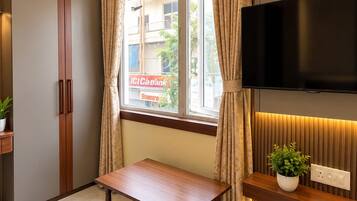 Quarto moderno com mesa de madeira, TV na parede e janela com cortinas.