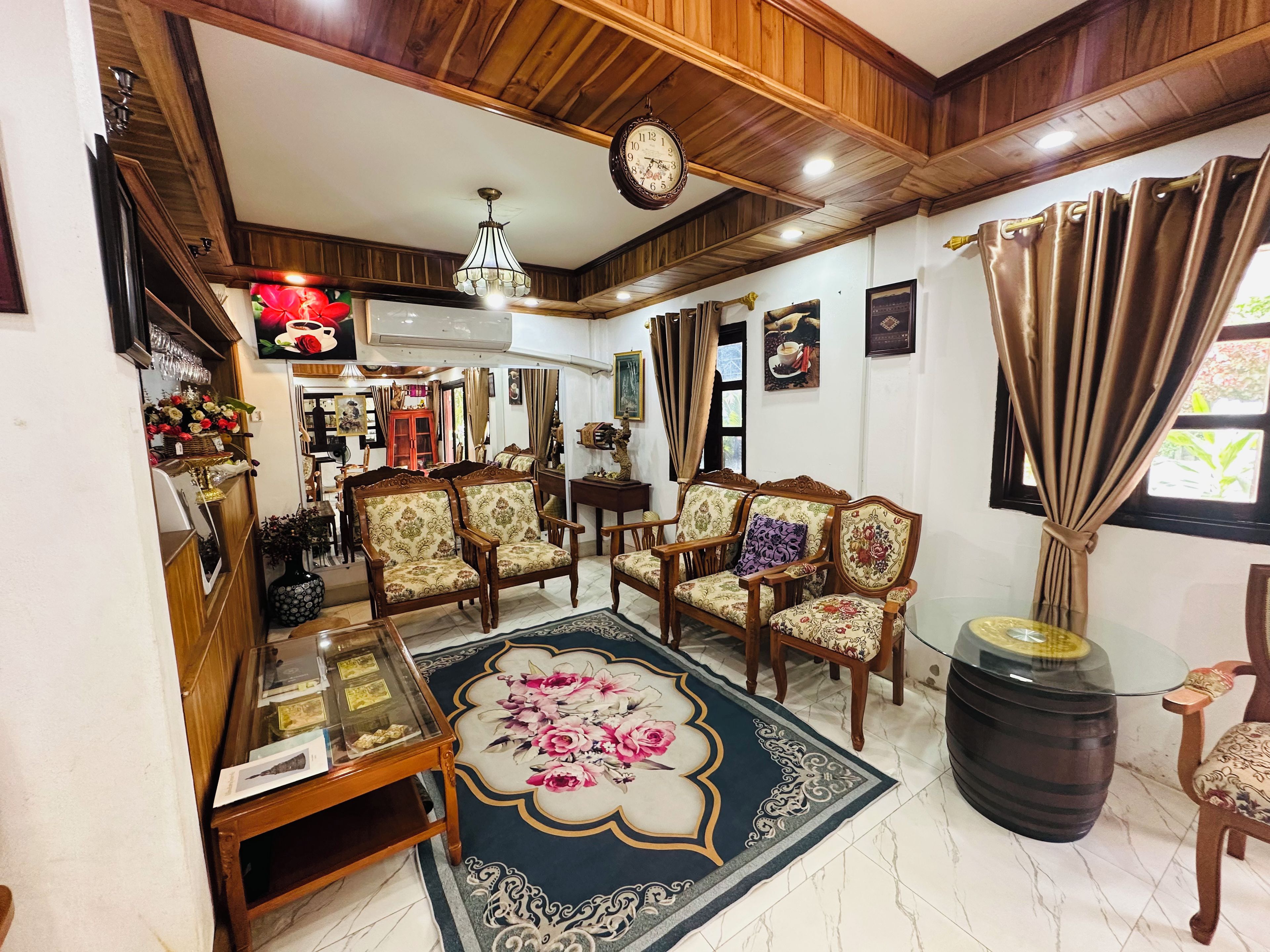Quarto com vigas de madeira no teto, um candelabro, um relógio e um tapete floral grande.