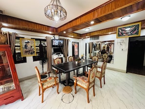 Uma sala de jantar com mesa preta e cadeiras de padrão floral, um ventilador de teto e um lustre.