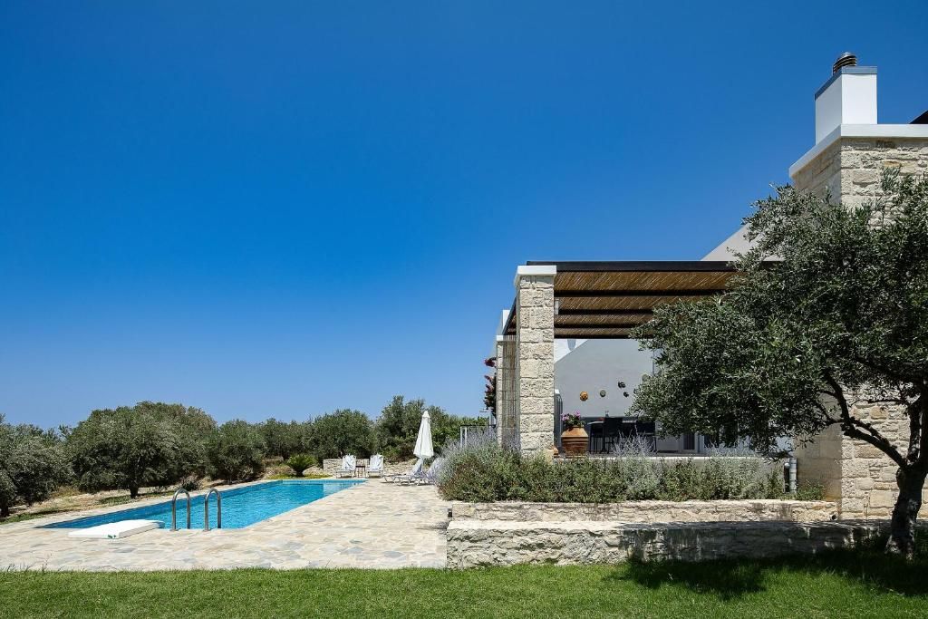 Um edifício de pedra com piscina, área de estar ao ar livre e oliveiras.