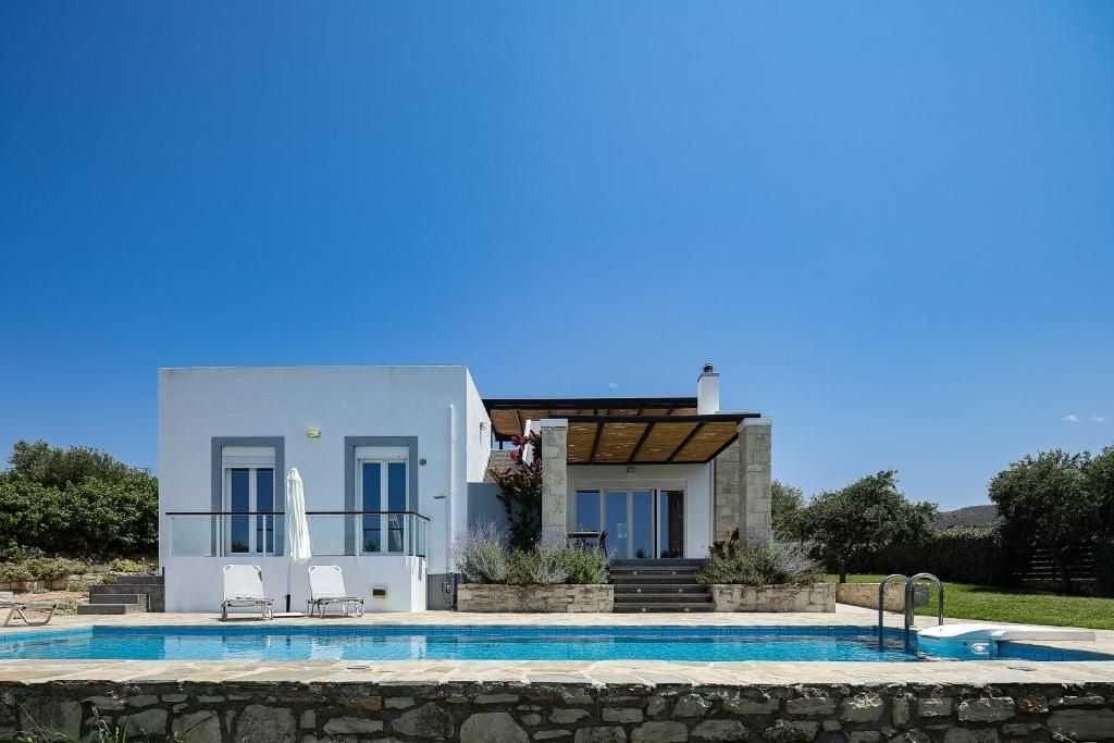 Uma casa moderna de dois andares com piscina, varanda coberta e muro de pedra.