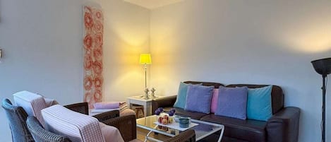 Uma sala de estar mobiliada com um sofá, poltronas, uma mesa de centro e um abajur.