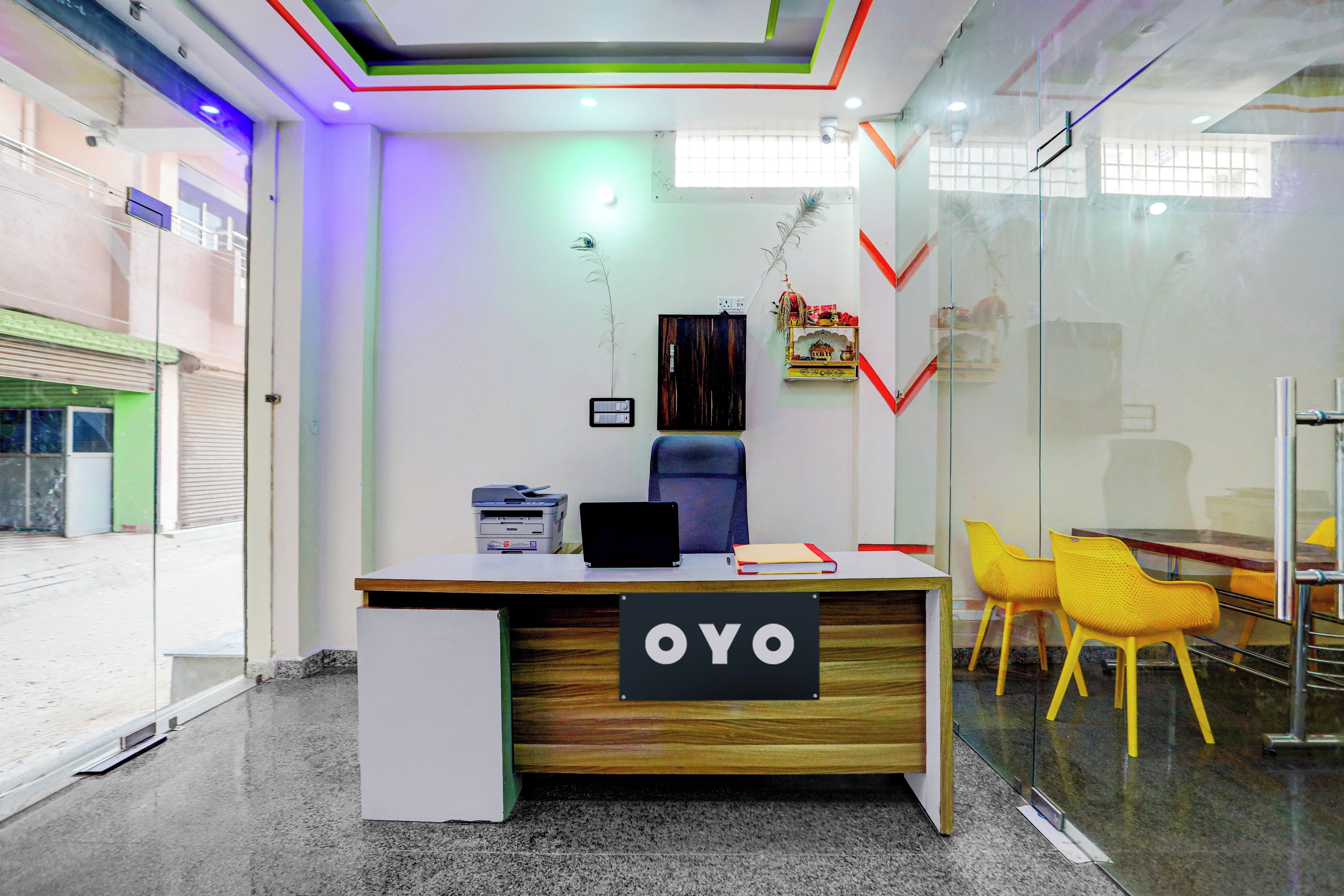 Escritório moderno com uma mesa de recepção identificada com 'OYO', uma impressora, um computador e um painel de vidro.