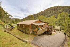 Uma cabana de madeira com varanda, rodeada por um morro coberto de árvores.