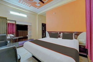 Quarto de hotel com uma cama grande, escrivaninha com cadeira, espelho e televisão.