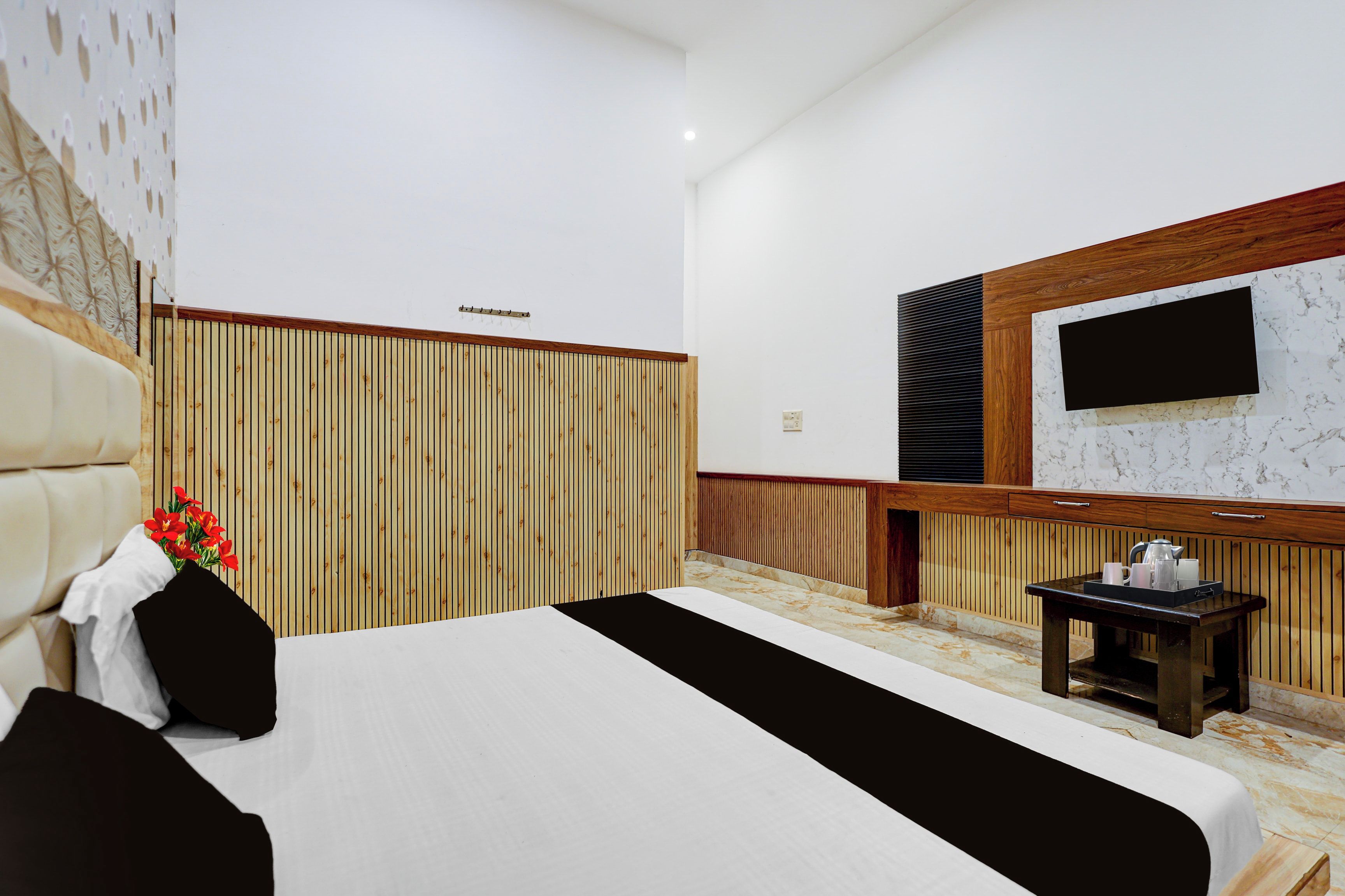 Quarto de hotel moderno com cama grande, painel de parede de madeira, televisão de tela plana e pequena mesa com bandeja.