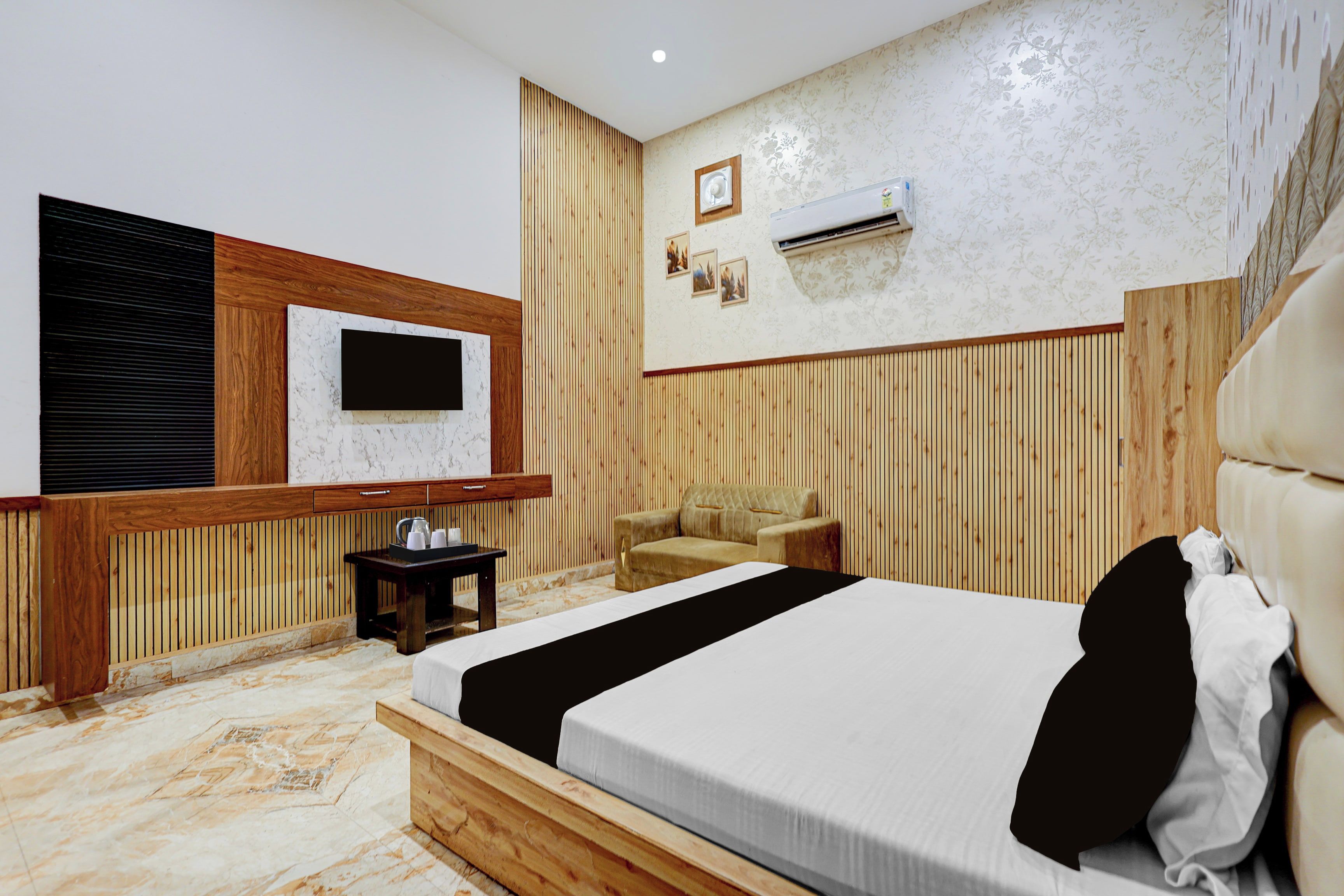 Quarto com cama, televisão na parede, painel de madeira e uma mesinha com chaleira.