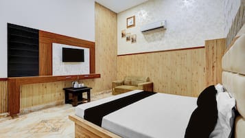 Quarto com cama, televisão na parede, painel de madeira e uma mesinha com chaleira.