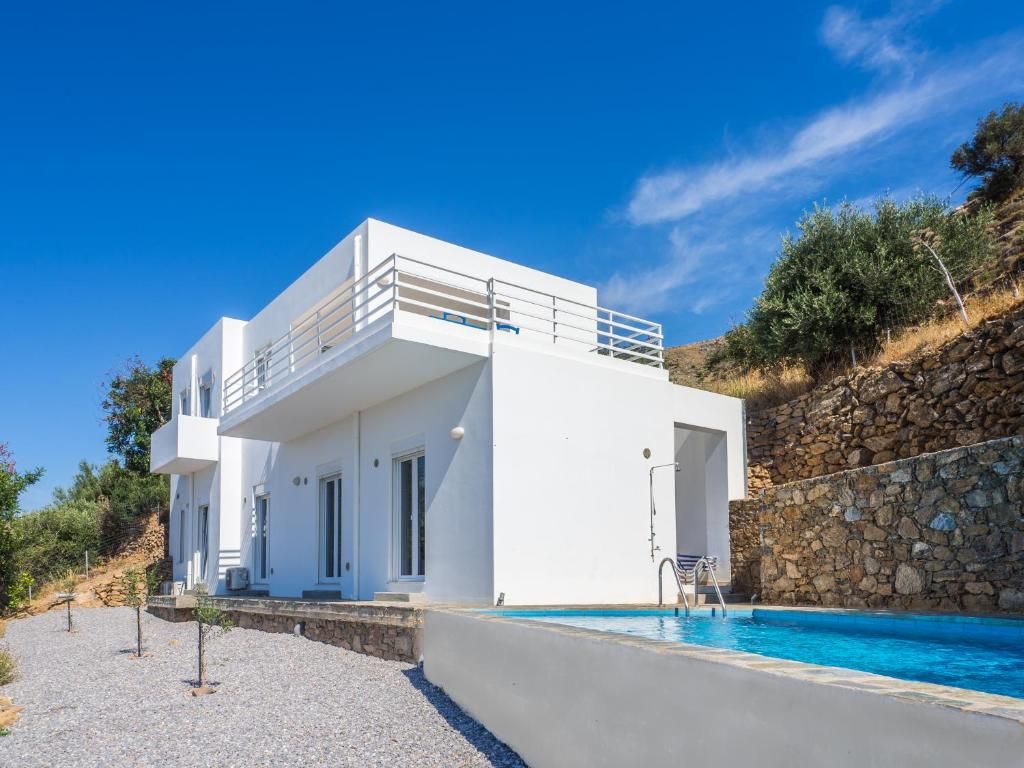 Uma vila moderna e branca com piscina, um muro de pedra e um céu azul límpido.