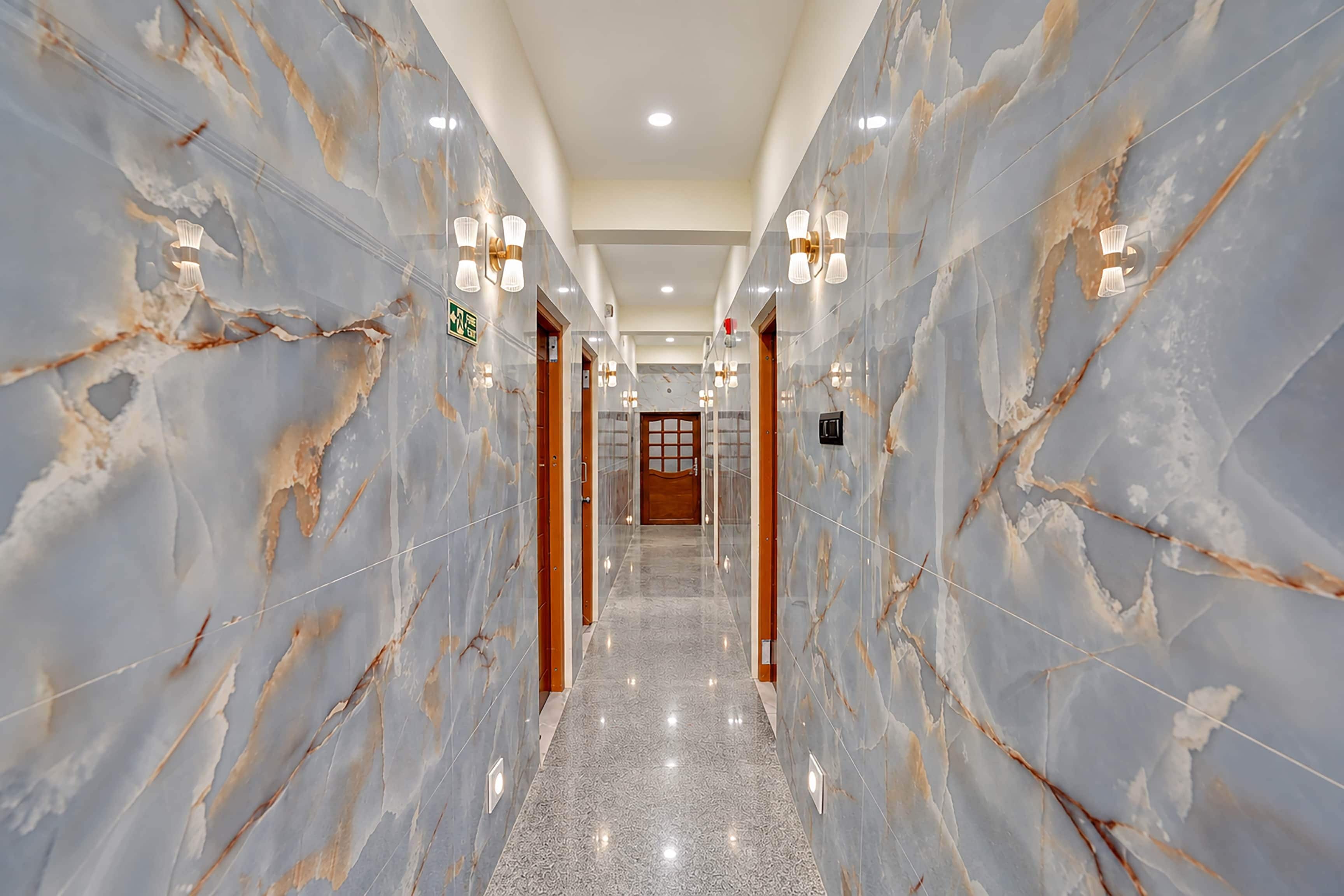 Um corredor com piso de mármore, luminárias e uma porta no final.