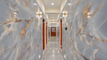 Um corredor com piso de mármore, luminárias e uma porta no final.