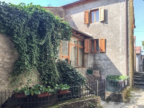 Um edifício com paredes cobertas de hera, uma porta de madeira e uma escadaria que leva a um andar superior.