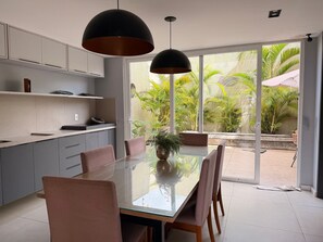 Uma cozinha moderna com uma mesa de jantar de vidro, cadeiras cor-de-rosa e iluminação pendente.
