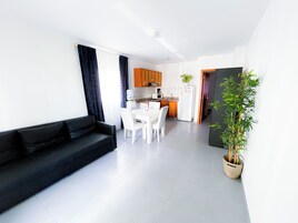 Uma sala de estar moderna com um sofá preto, uma mesa de jantar com cadeiras, e uma cozinha com armários de madeira e eletrodomésticos.