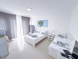 Quarto de hotel com cama, escrivaninha, cadeira, televisão e janela com cortinas.