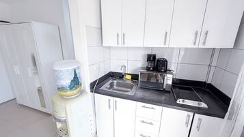 Uma cozinha moderna com armários brancos, bancada preta, pia, máquina de café e dispensador de água.
