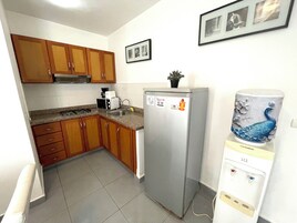 Cozinha compacta com armários de madeira, geladeira de aço inoxidável, dispenser de água e micro-ondas.
