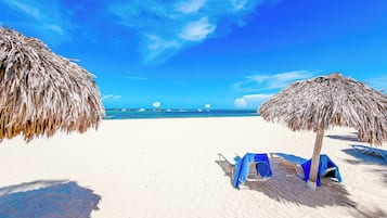 Uma praia com guarda-sóis de palha, areal arenoso e céu azul límpido.