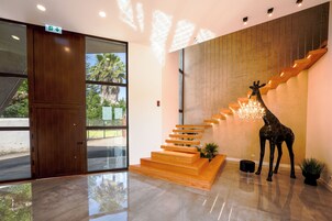 Interior moderno com escada de madeira, escultura de girafa e porta de vidro que dá para o exterior.