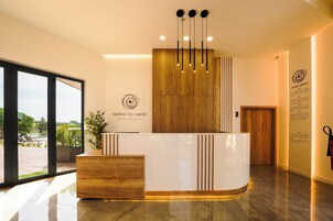 Balcão de recepção com painel de madeira ao fundo, um logotipo e uma parede com texto.