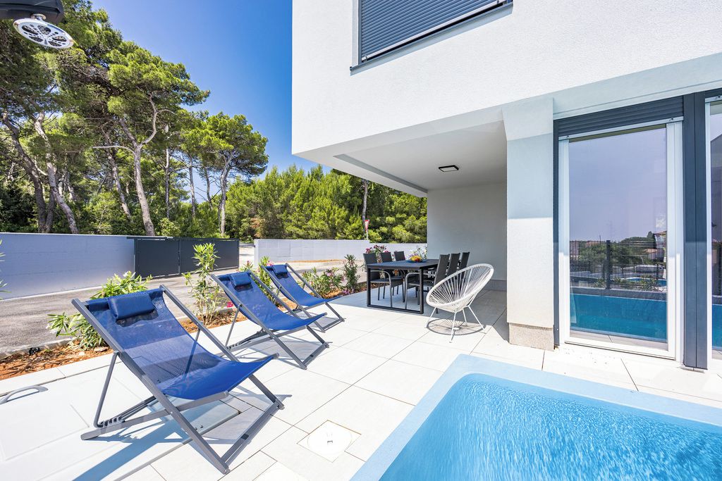 Uma área moderna com piscina ao ar livre, cadeiras de descanso, mesa de jantar e vista para a paisagem circundante.
