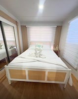 Quarto de hotel com cama, mesa de cabeceira, espelho e janela com persianas.