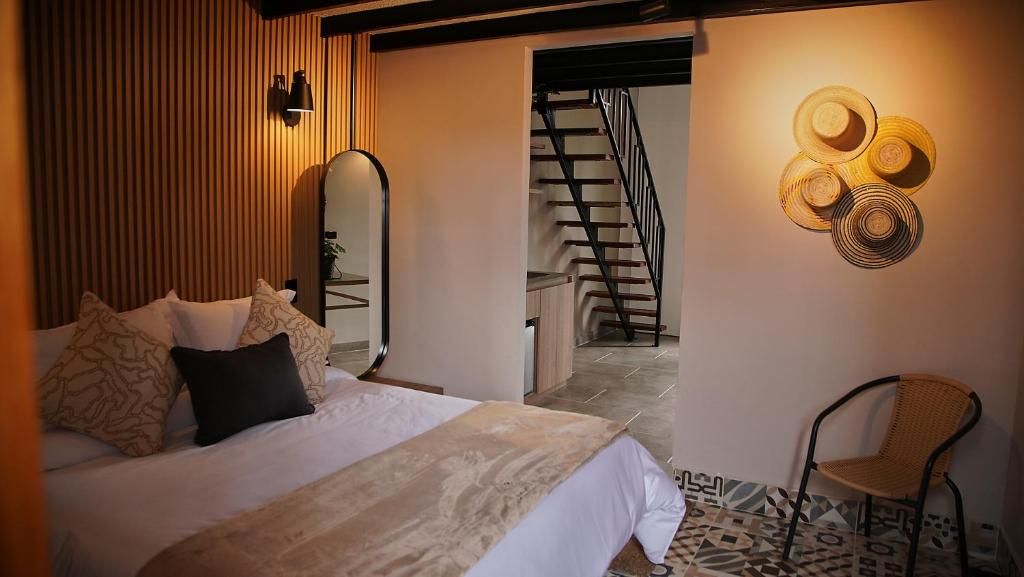Quarto com cama, espelho, expositor de chapéus na parede, cadeira e escada que leva a outro cômodo.