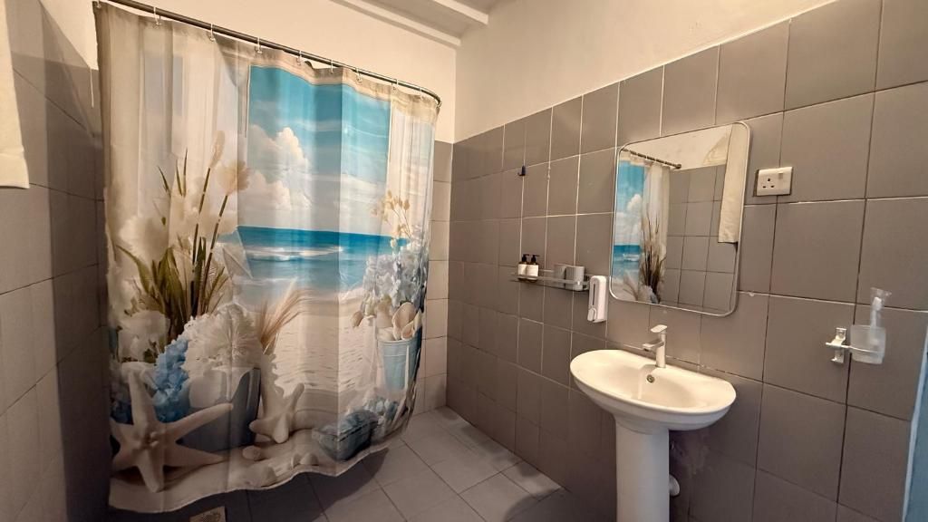 Casa de banho com cortina de chuveiro ilustrada com uma cena de praia, uma pia e um espelho.