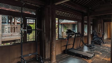 Academia com equipamentos de ginástica, vigas de madeira e janelas amplas.