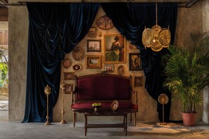 Quarto com um banco estofado em vermelho, parede decorada com obras de arte emolduradas e luminária pendente.