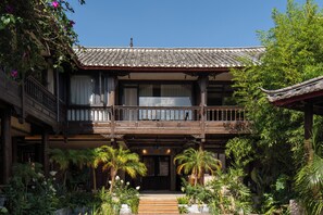 Um edifício tradicional com telhado em azulejos, varanda e jardim com diversas plantas.