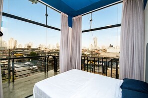 Quarto de hotel com cama, janelas amplas e vista para a cidade.
