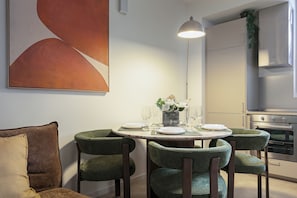 Uma zona de refeições moderna com uma mesa redonda, quatro cadeiras estofadas, uma luz pendente e um grande quadro abstrato na parede.