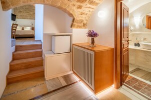 Um interior moderno com um arco de pedra que dá para um quarto, um pequeno radiador branco e um banheiro com uma pia grande e piso de azulejos.