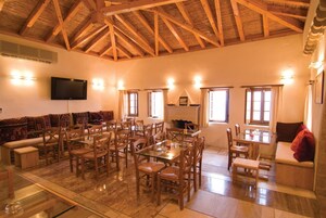 Uma sala de estar ampla com teto de madeira alto, TV de tela plana na parede e área de jantar com cadeiras e mesas de madeira.